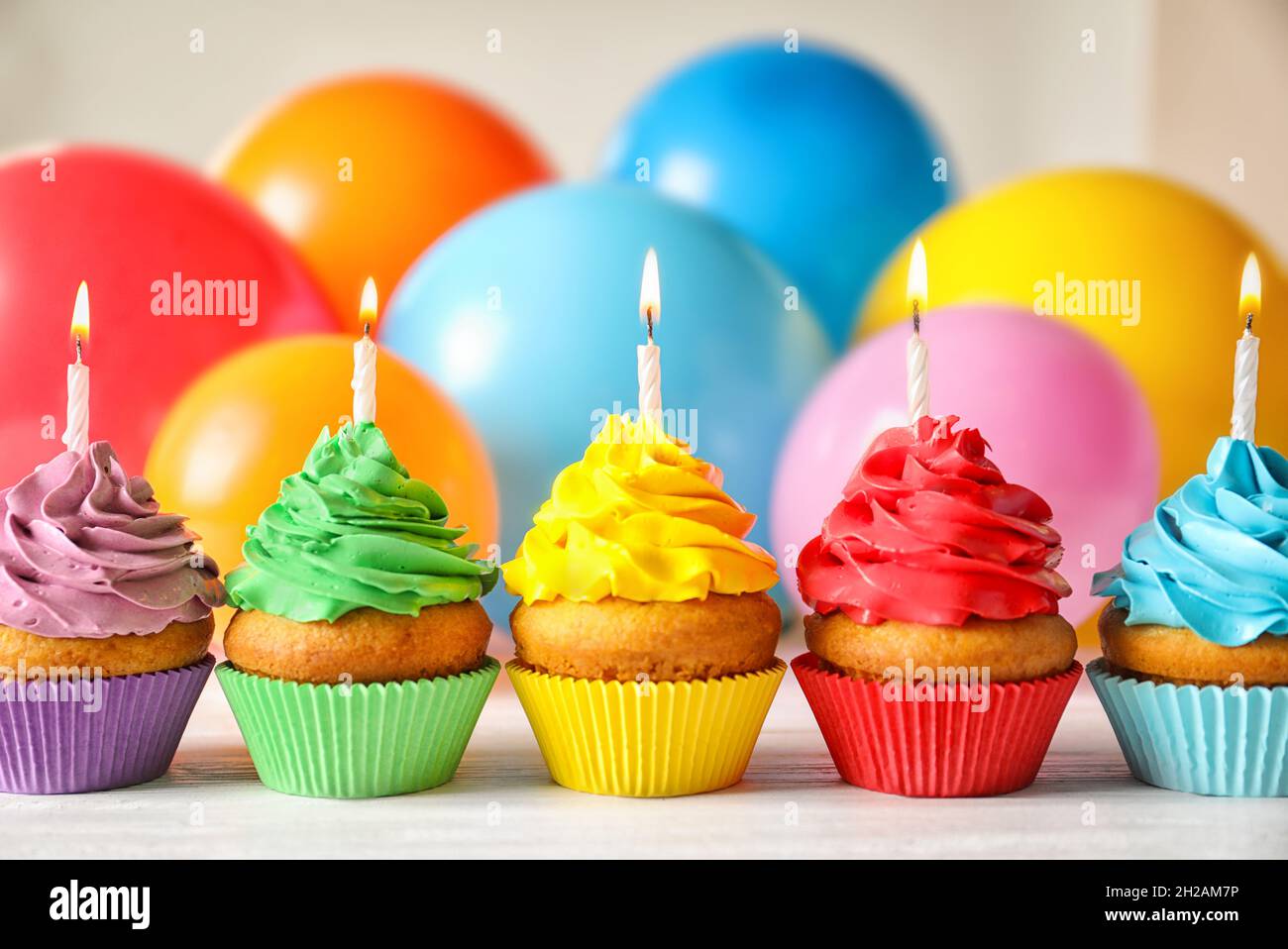 Delicious birthday cupcakes with candles and blurred balloons on ...
