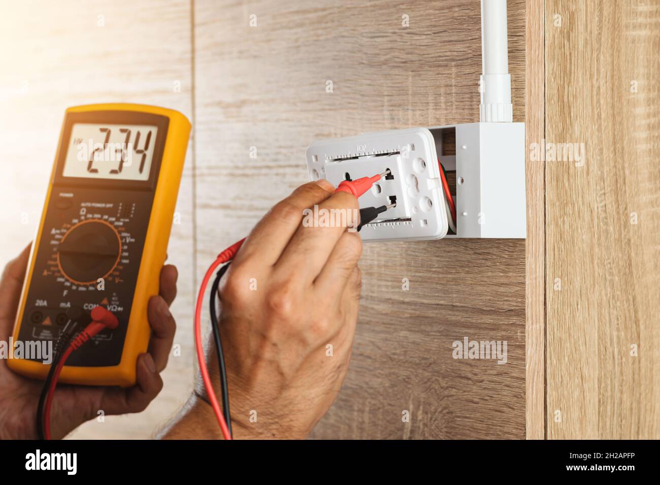 Electrician using a digital meter to measure the voltage at a wall ...