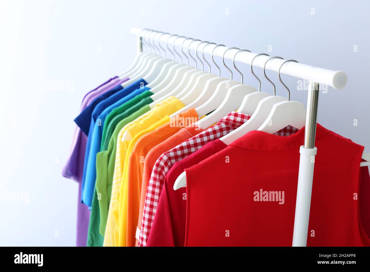 Rack with rainbow clothes on light background Stock Photo - Alamy