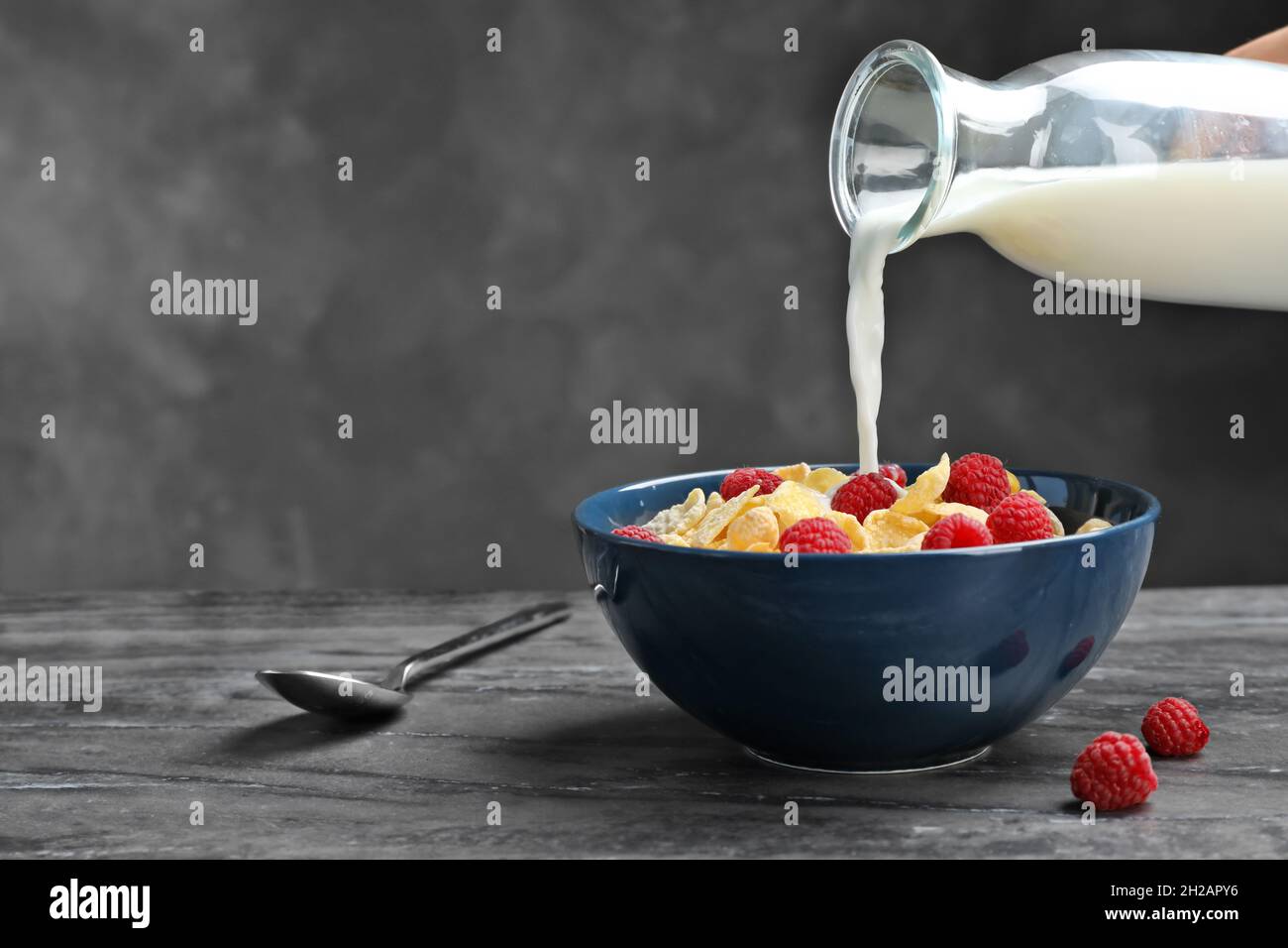 Pouring milk into bowl with cornflakes on dark table. Whole grain cereal for breakfast Stock ...