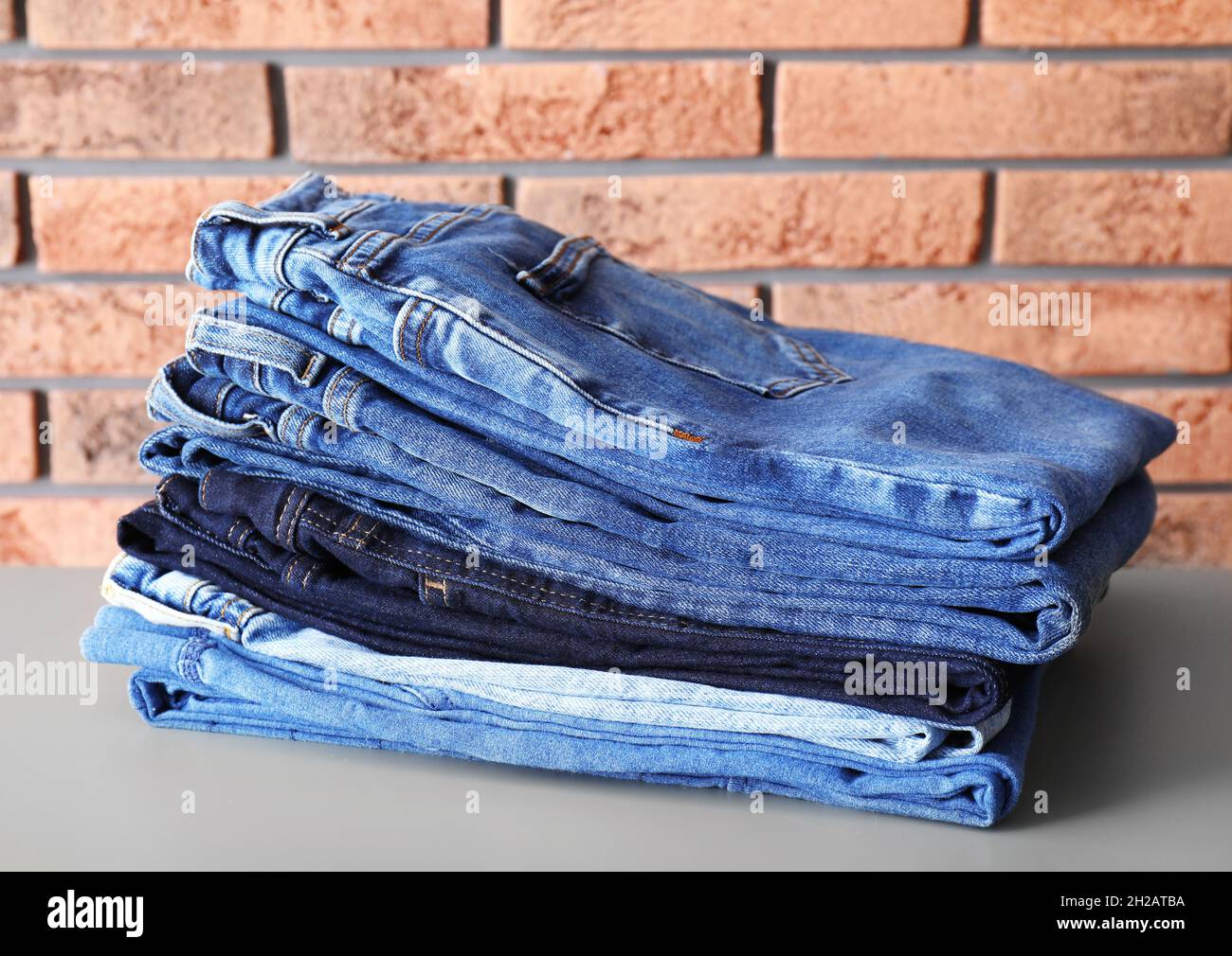 Stack of jeans on table against brick wall background Stock Photo - Alamy