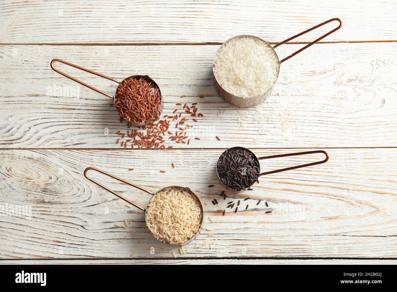 Measuring cups with different types of rice on white wooden background ...