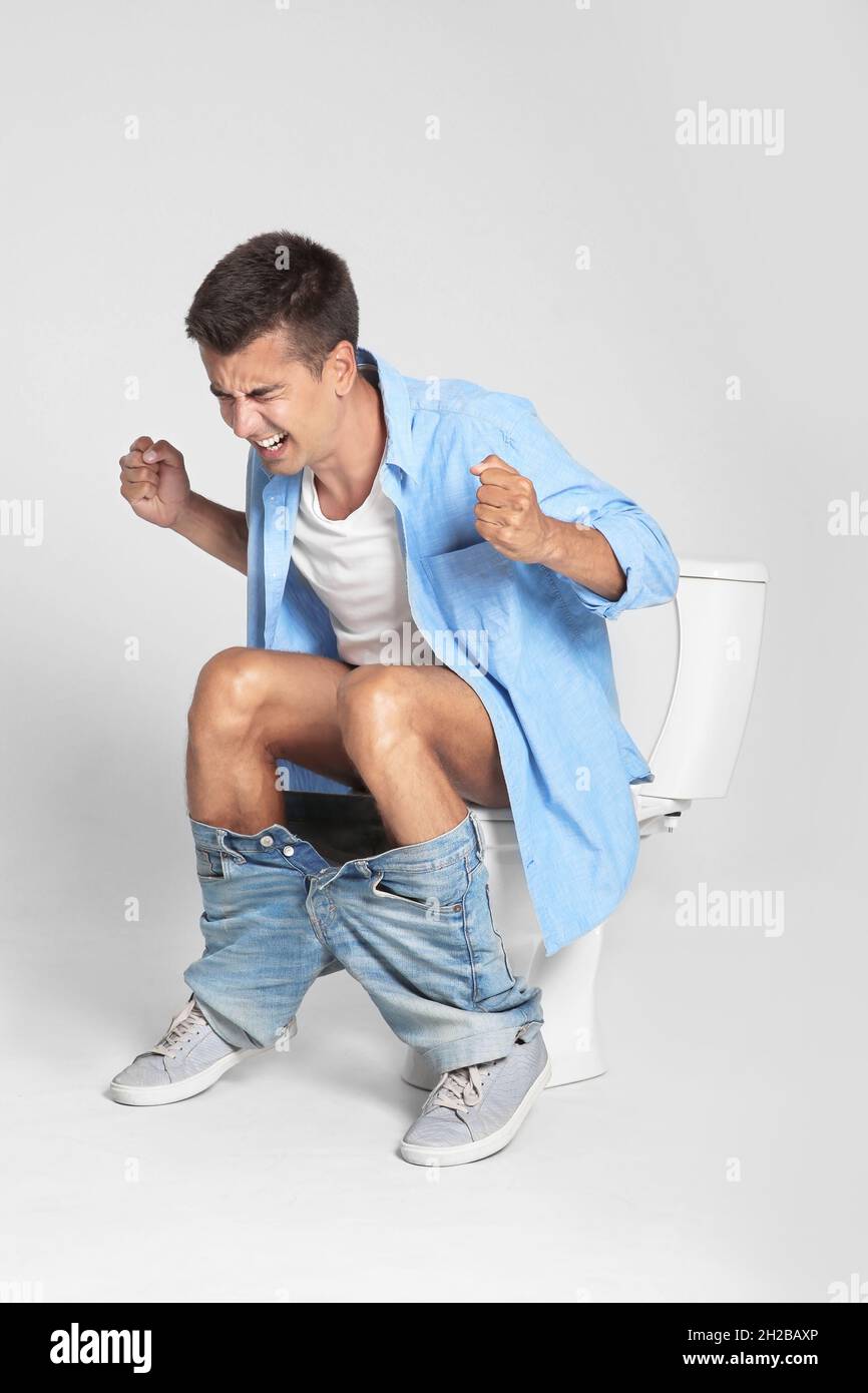 Young man suffering from diarrhea on toilet bowl against gray ...