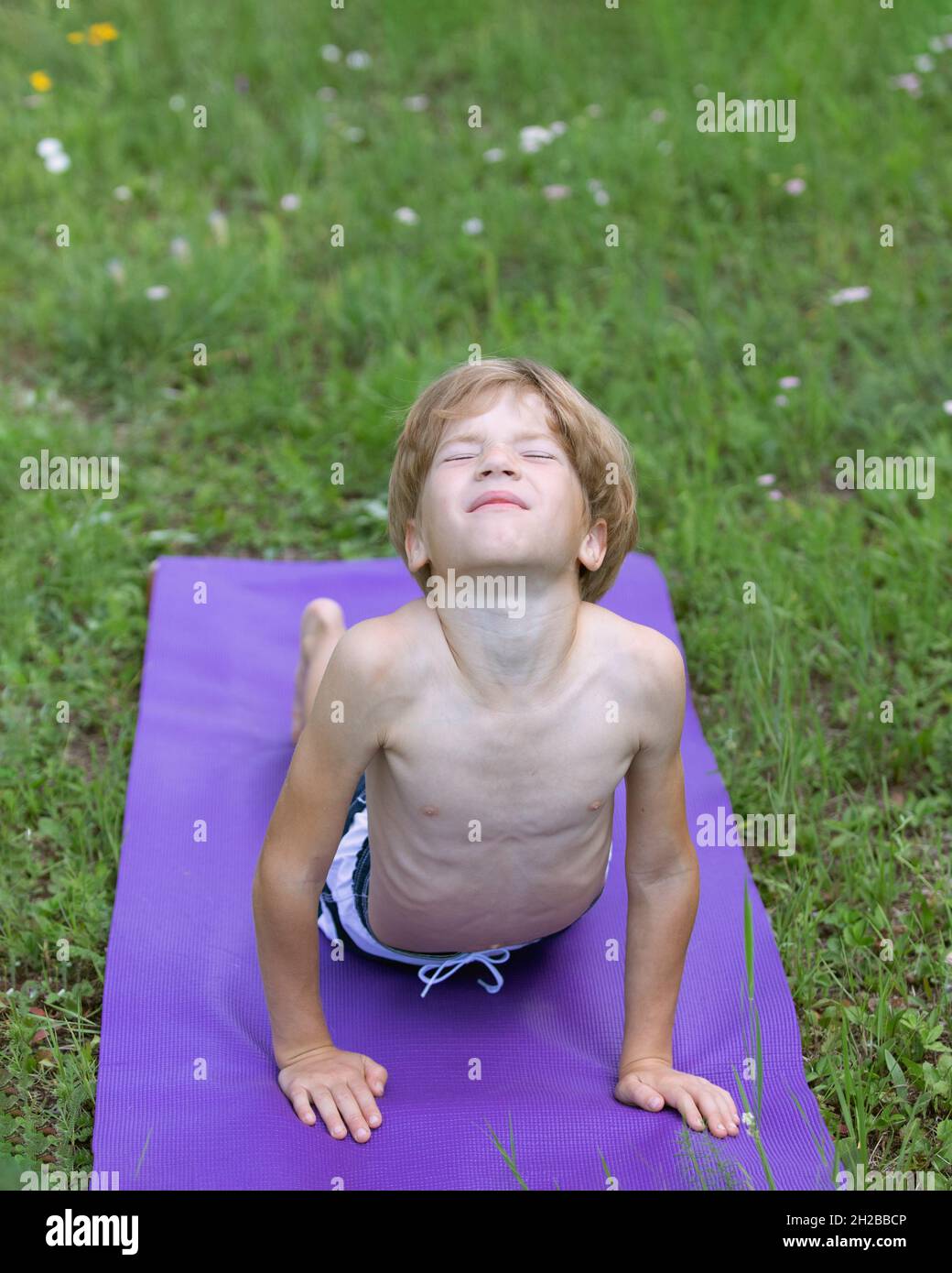 Little caucasian boy doing yoga cobra position outside on open air ...