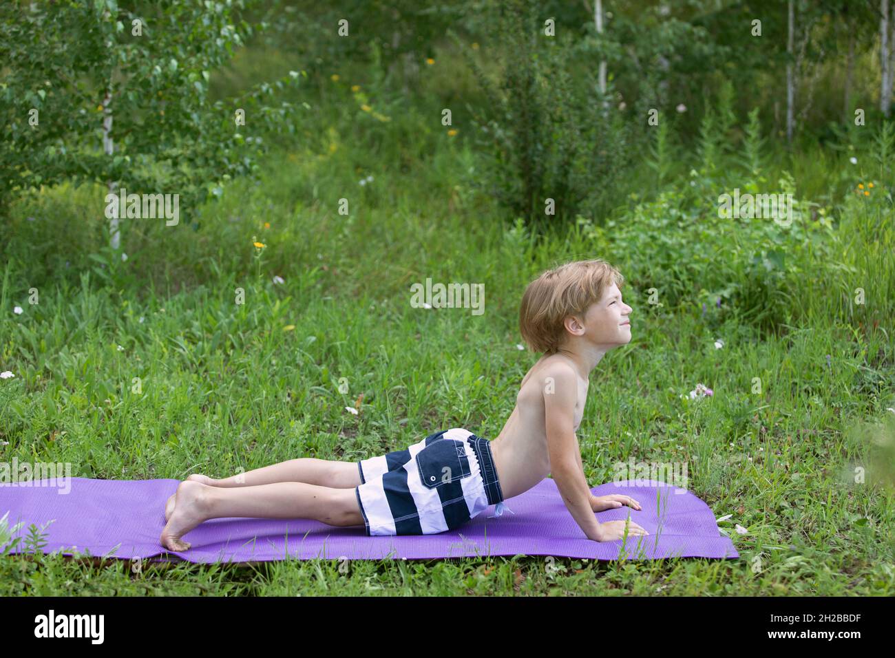 Little caucasian boy doing yoga cobra position outside on open air ...