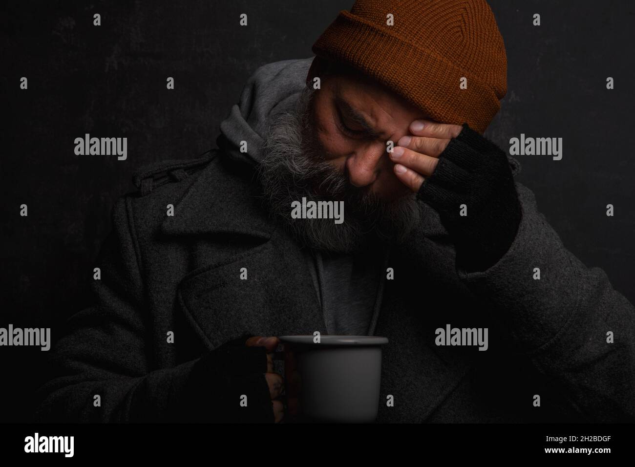 Sad homeless man with a gray beard holding a cup of hot tea to warm ...