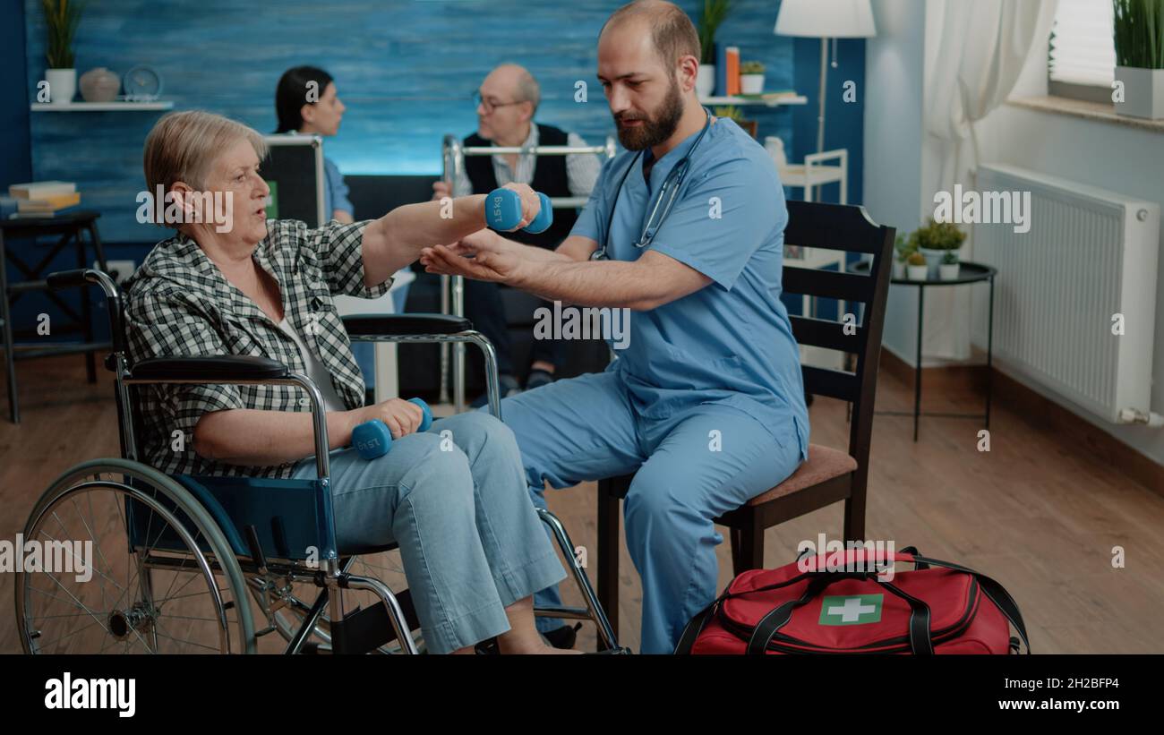 Medical assistant helping disabled woman with physical exercises in ...