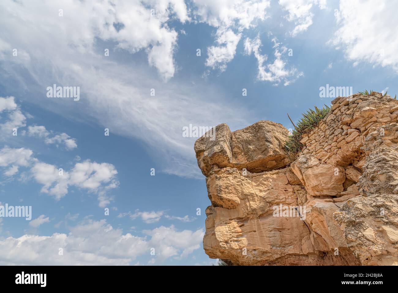 Low angle shot of a cliff on the background of blue sky with fluffy ...