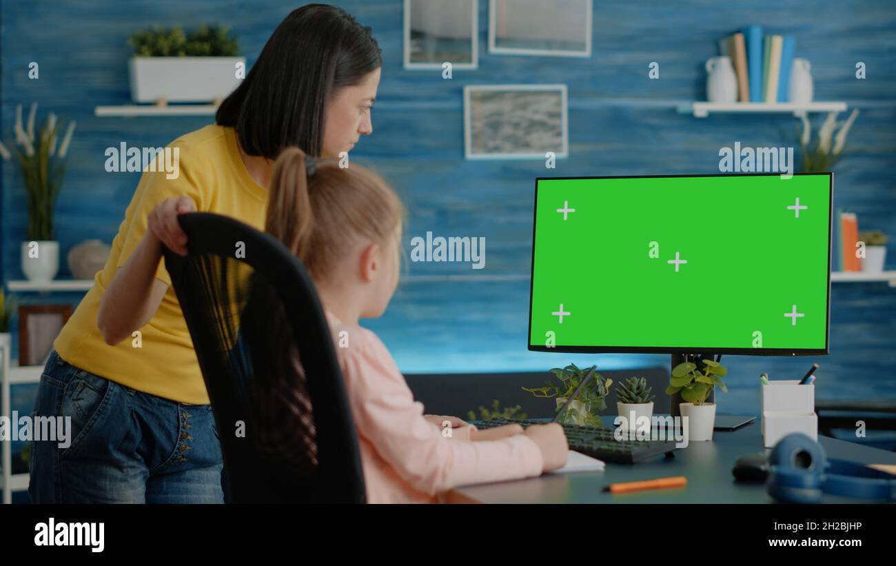 Mother and daughter looking at horizontal green screen on computer at ...
