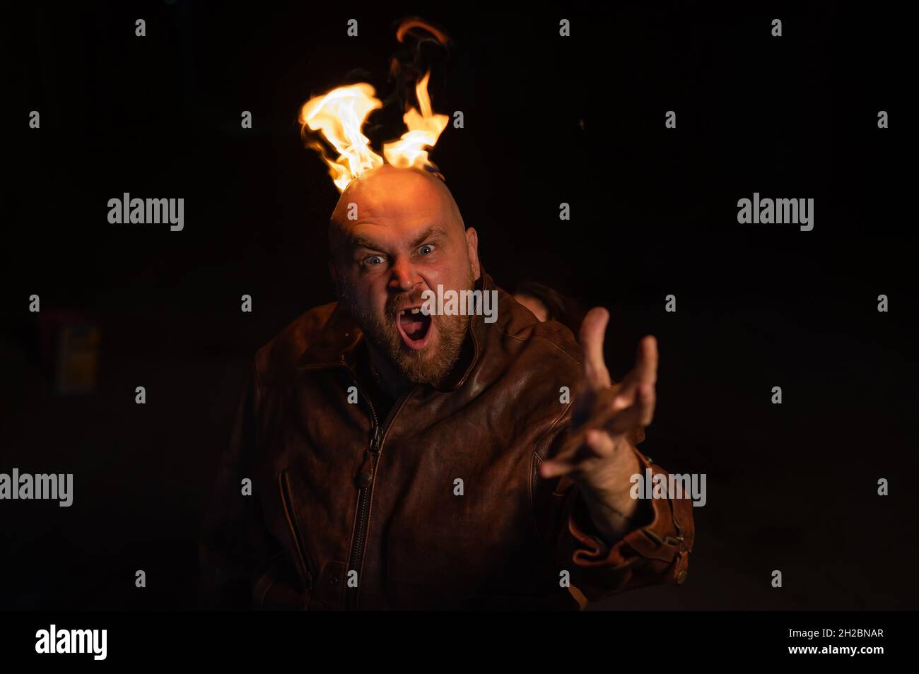 Bald man in a leather jacket with a burning head on a dark background ...