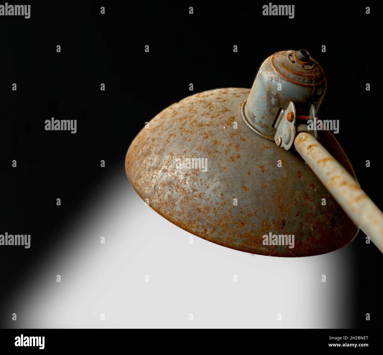 Rusty old weathered desk lamp with white cone of light from its shade ...