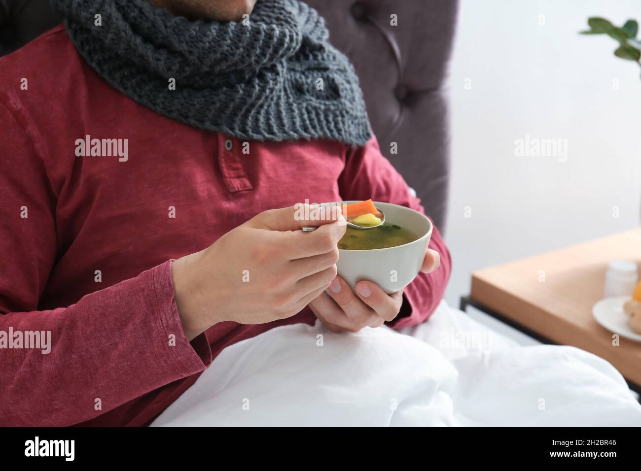Sick young man eating broth to cure cold in bed at home Stock Photo - Alamy