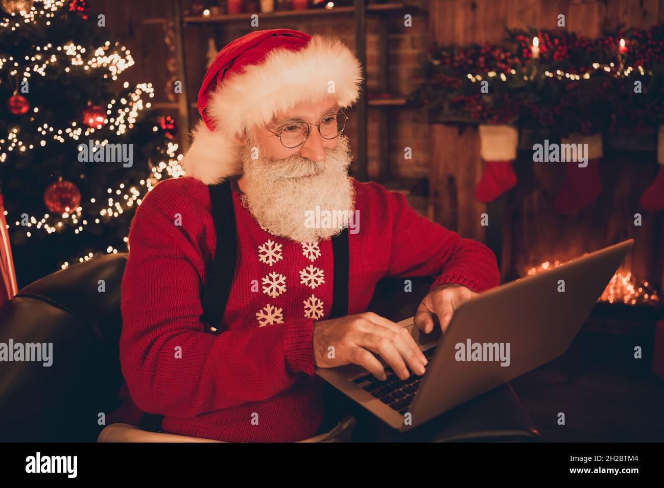 Photo of cheerful glad santa claus look sit workplace work laptop wear ...