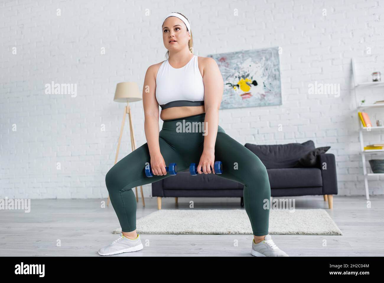 Plus size woman doing squat while training with dumbbells at home Stock ...