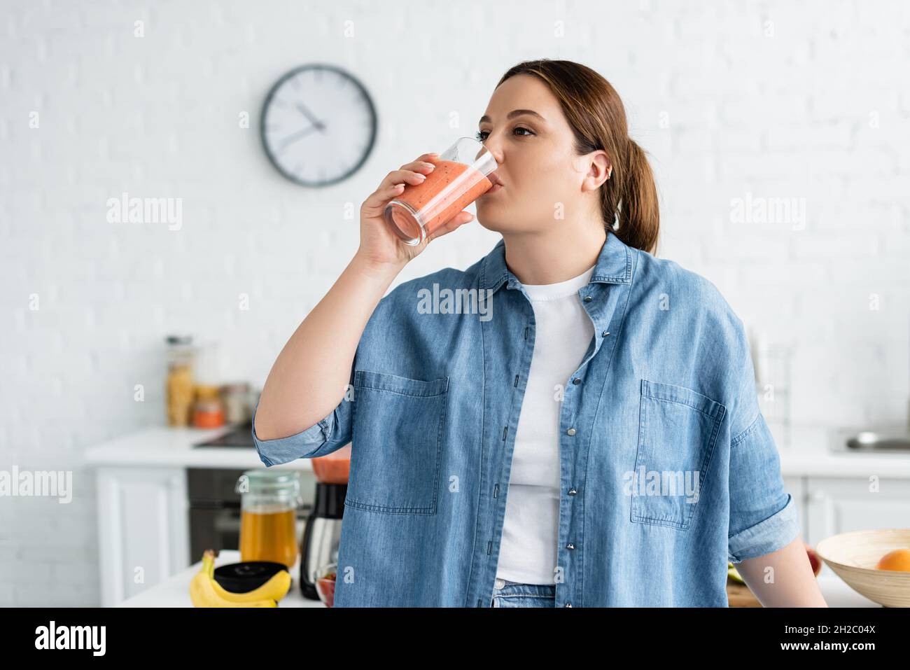 Plus size woman drinking fruit smoothie in kitchen Stock Photo - Alamy