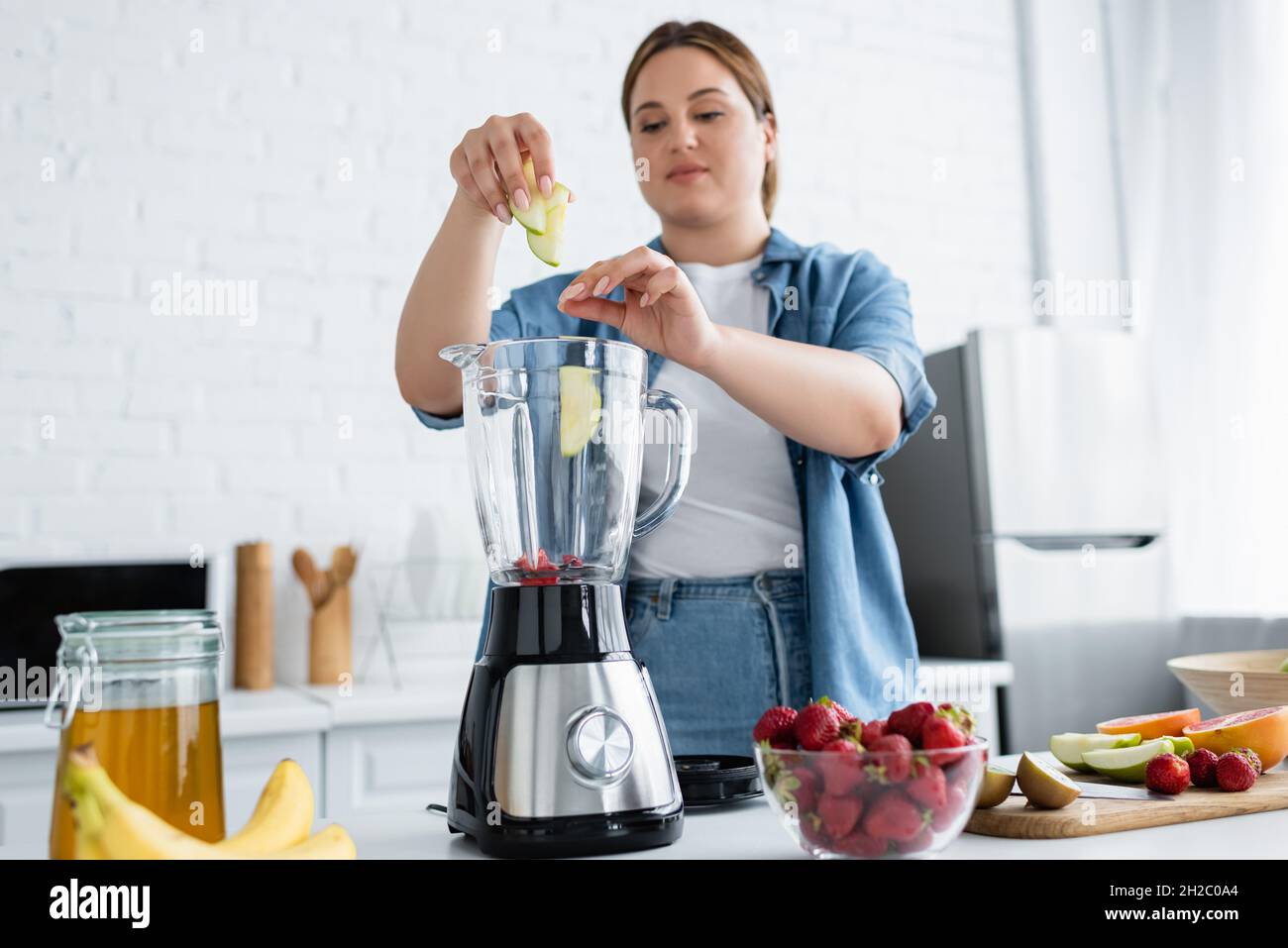 Blurred woman with overweight cooking smoothie in blender in kitchen ...