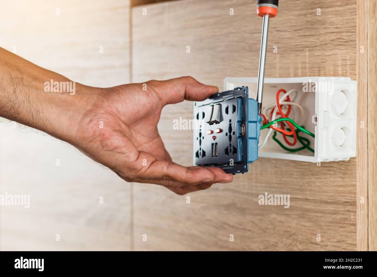 Hand of an electrician is using a screwdriver to attach the wires to ...
