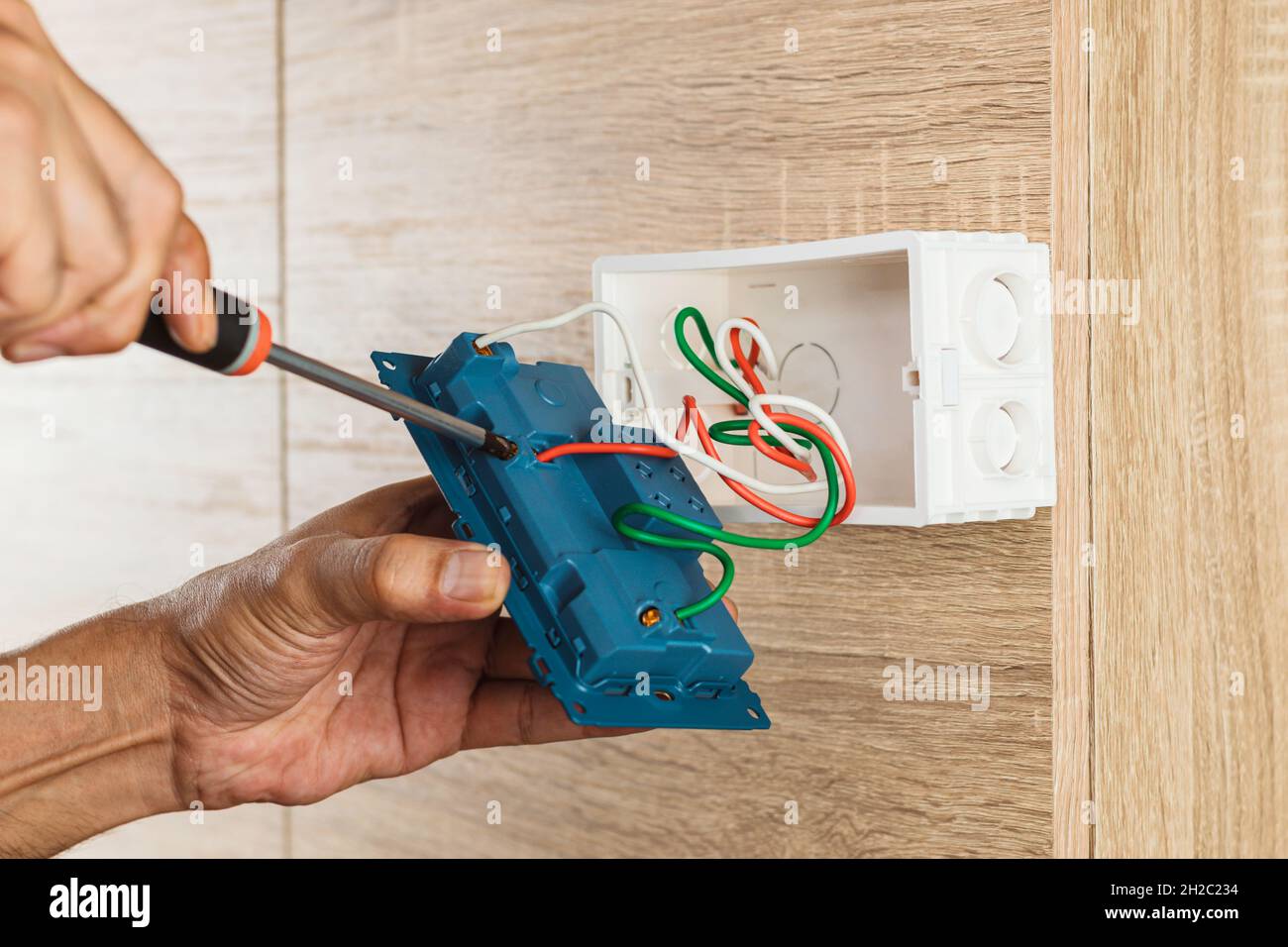 Hand of an electrician is using a screwdriver to attach the wires to ...