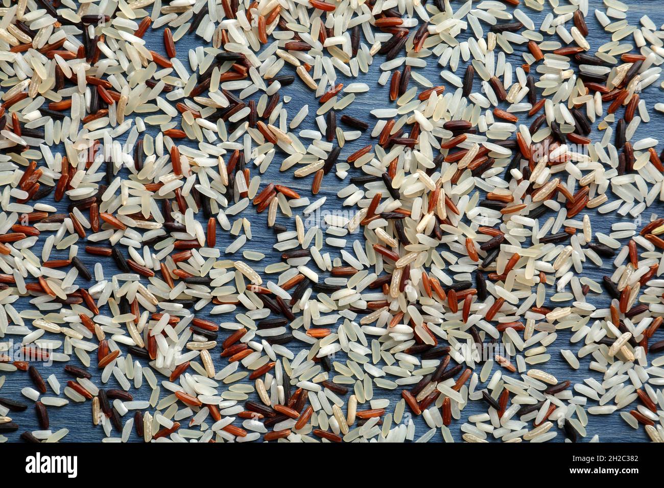 Brown and other types of rice scattered on color wooden background ...