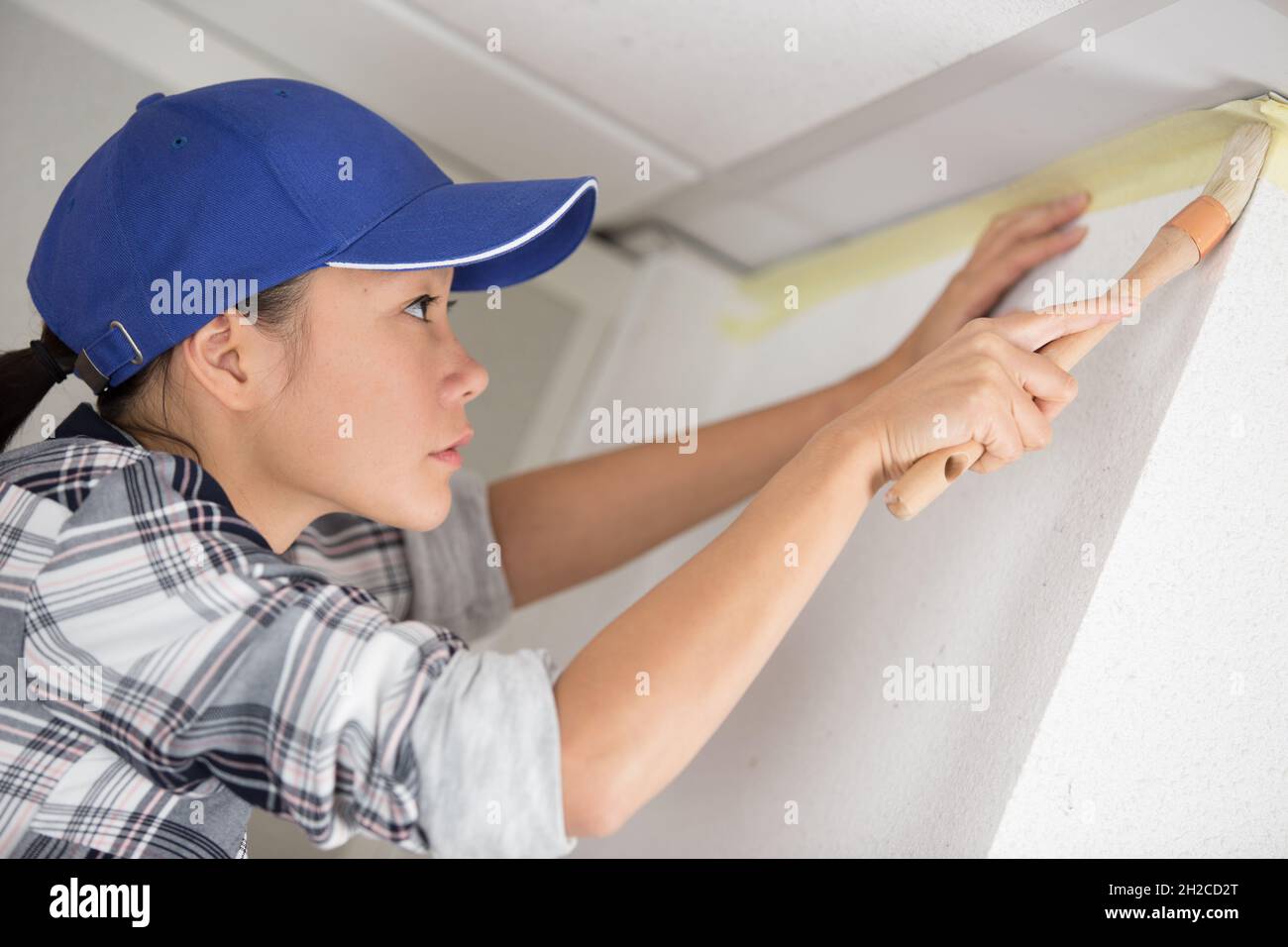 female decorator pressing masking tape to ceiling with a brush Stock ...