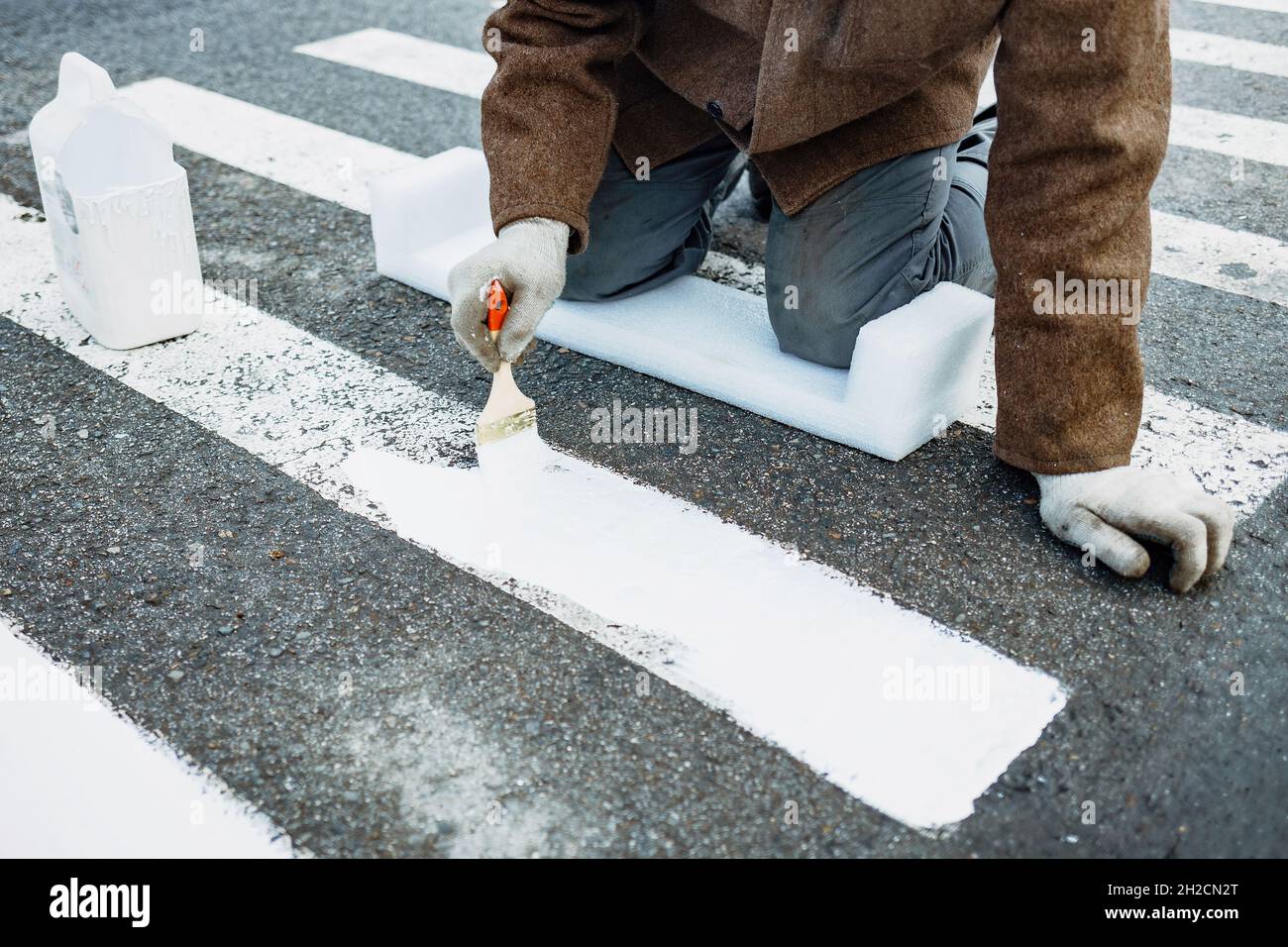 A man paints with a brush on the asphalt markings for a pedestrian ...