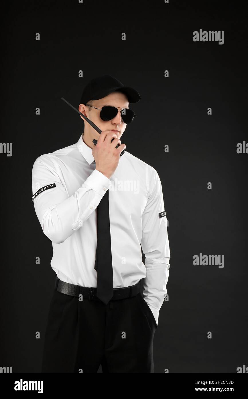 Male security guard using portable radio transmitter on dark background ...