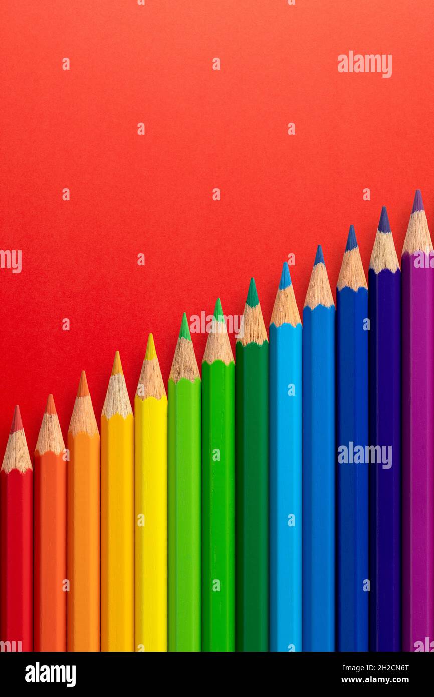 Colour pencils arranged diagonally on a red vertical paper background ...