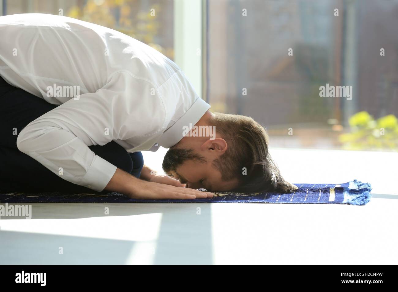 Muslim man in suit praying on rug indoors Stock Photo - Alamy