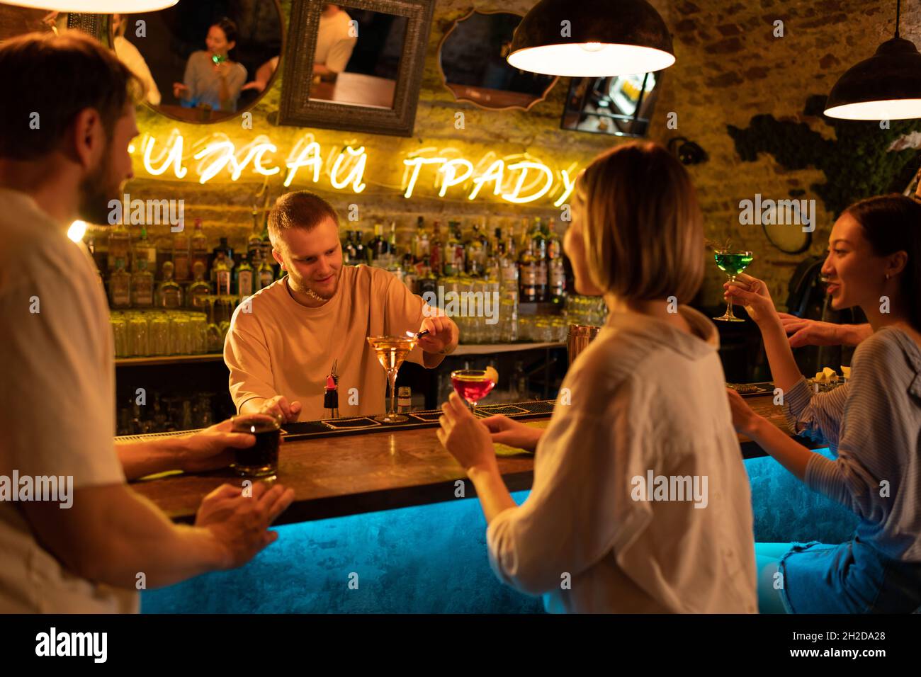Male barkeeper igniting alcohol drink on counter near clients while ...