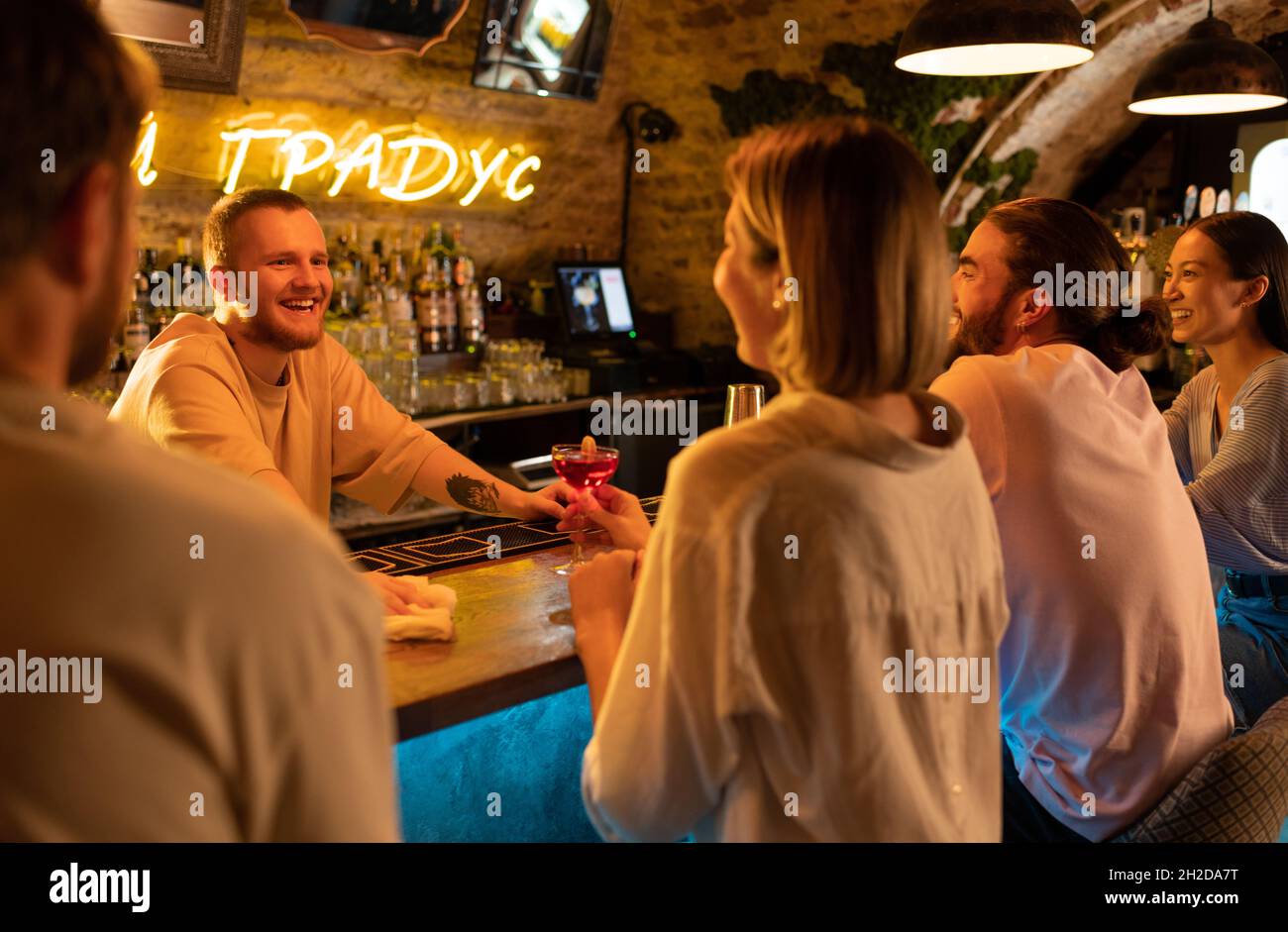 Happy bartender smiling and chatting with diverse clients while serving ...