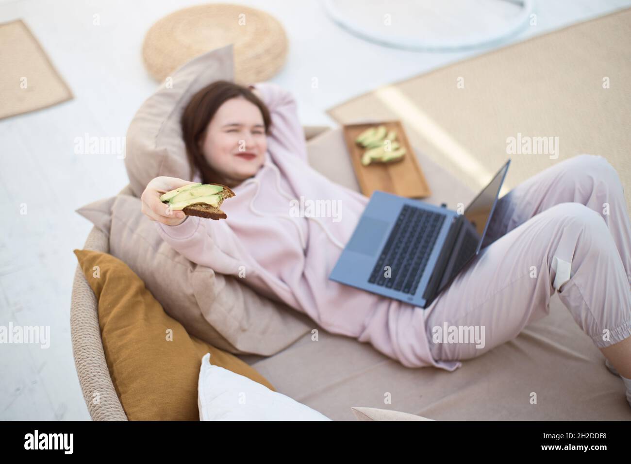 Woman works on laptop and holds out toast with avocado Stock Photo - Alamy
