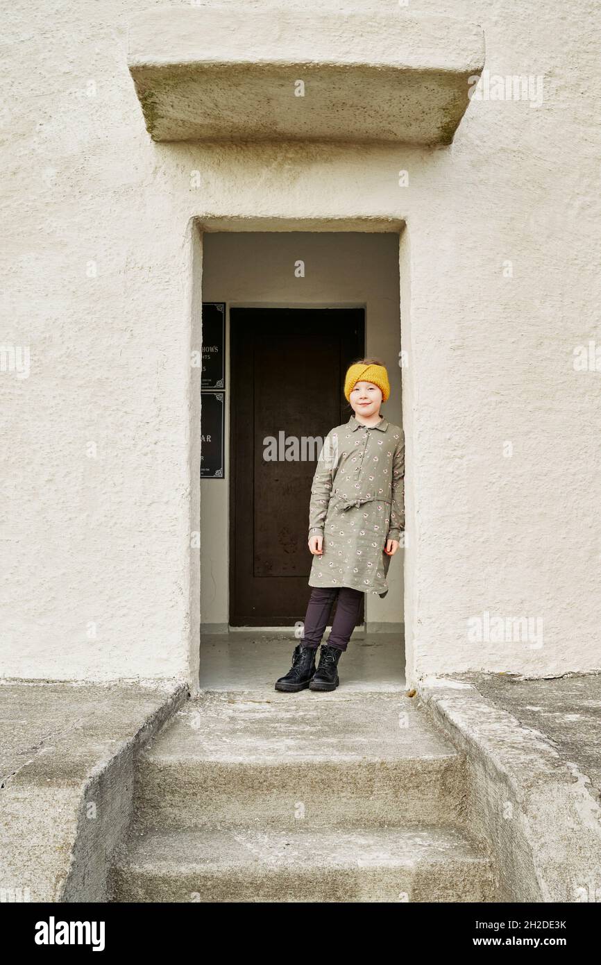 Cute child standing in doorway of white concrete house in countryside ...