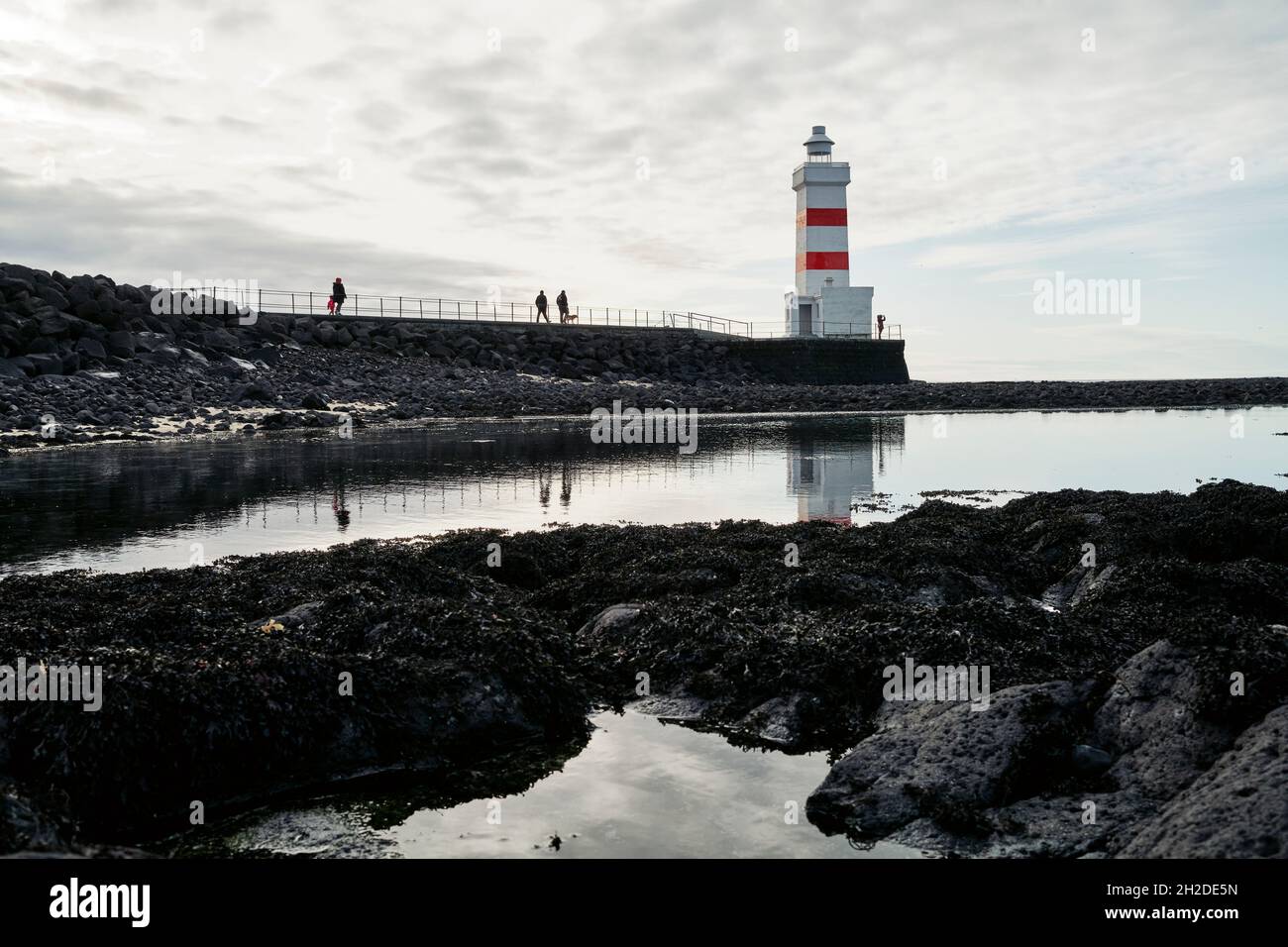 Distant view of red and white beacon tower located on coast near sea in ...
