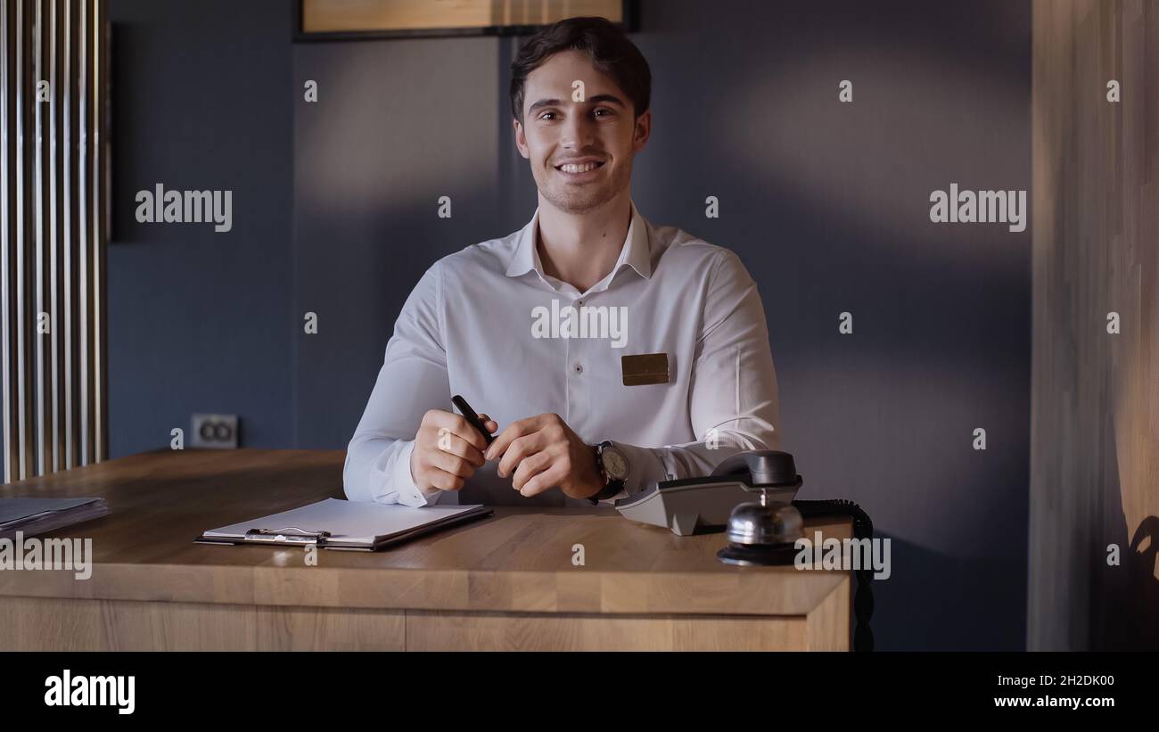 happy receptionist looking at camera while standing at reception ...