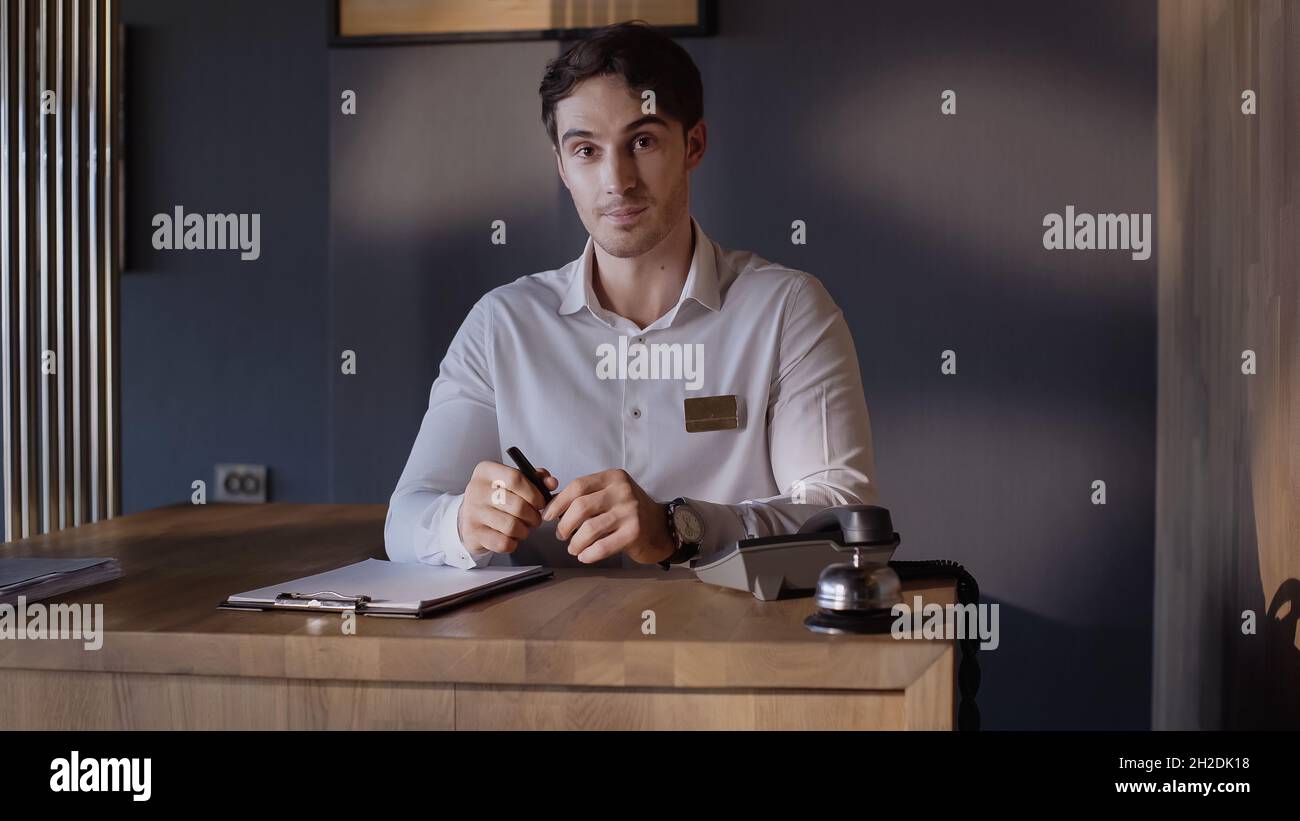 young receptionist looking at camera while standing at reception ...