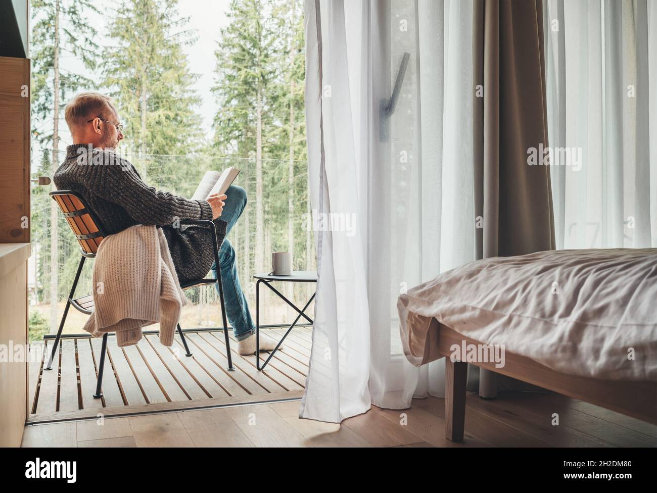 Alone man sitting in chair on country house balcony and enjoying forest ...