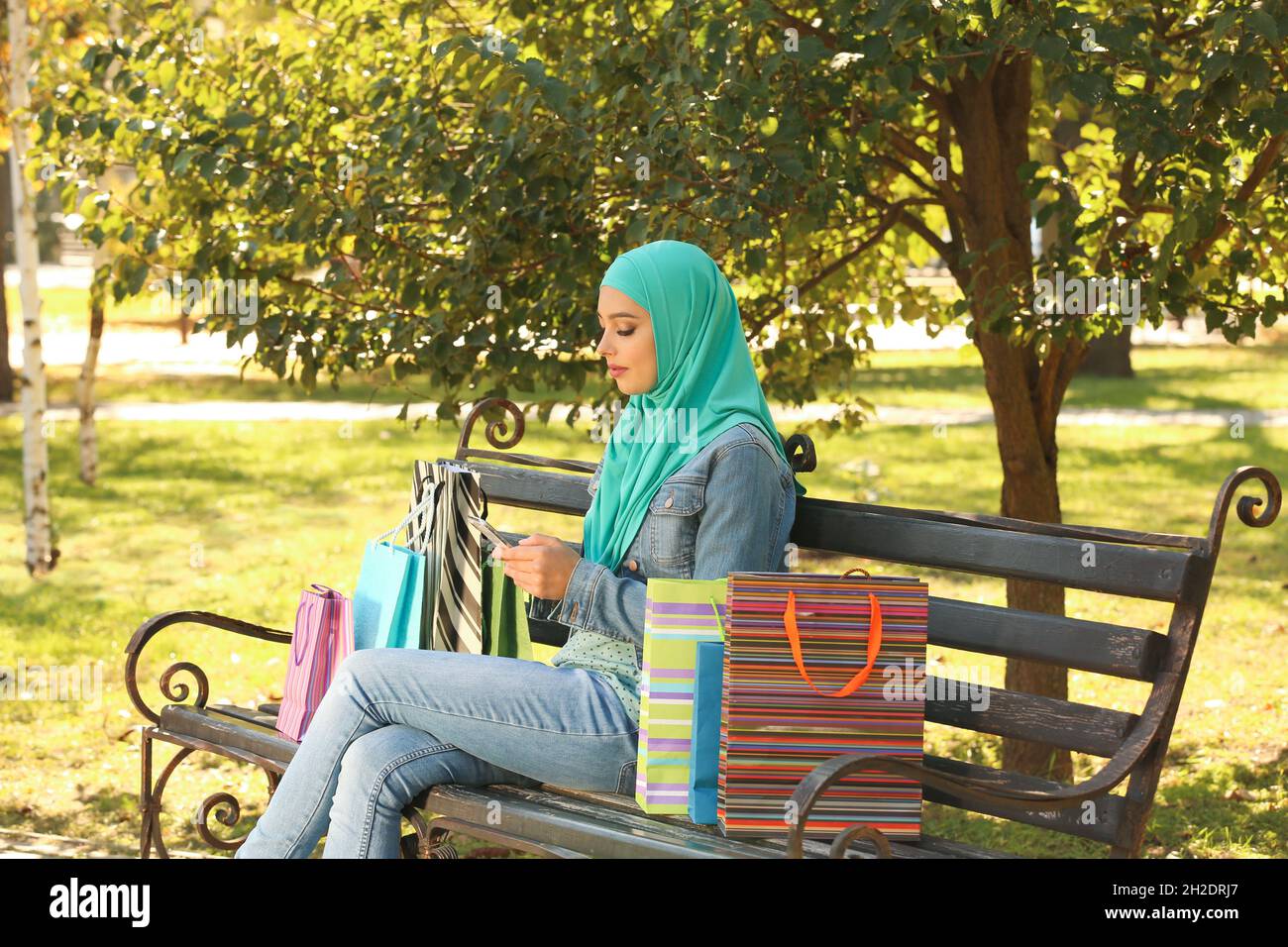 Muslim woman with mobile phone sitting on bench in park Stock Photo - Alamy
