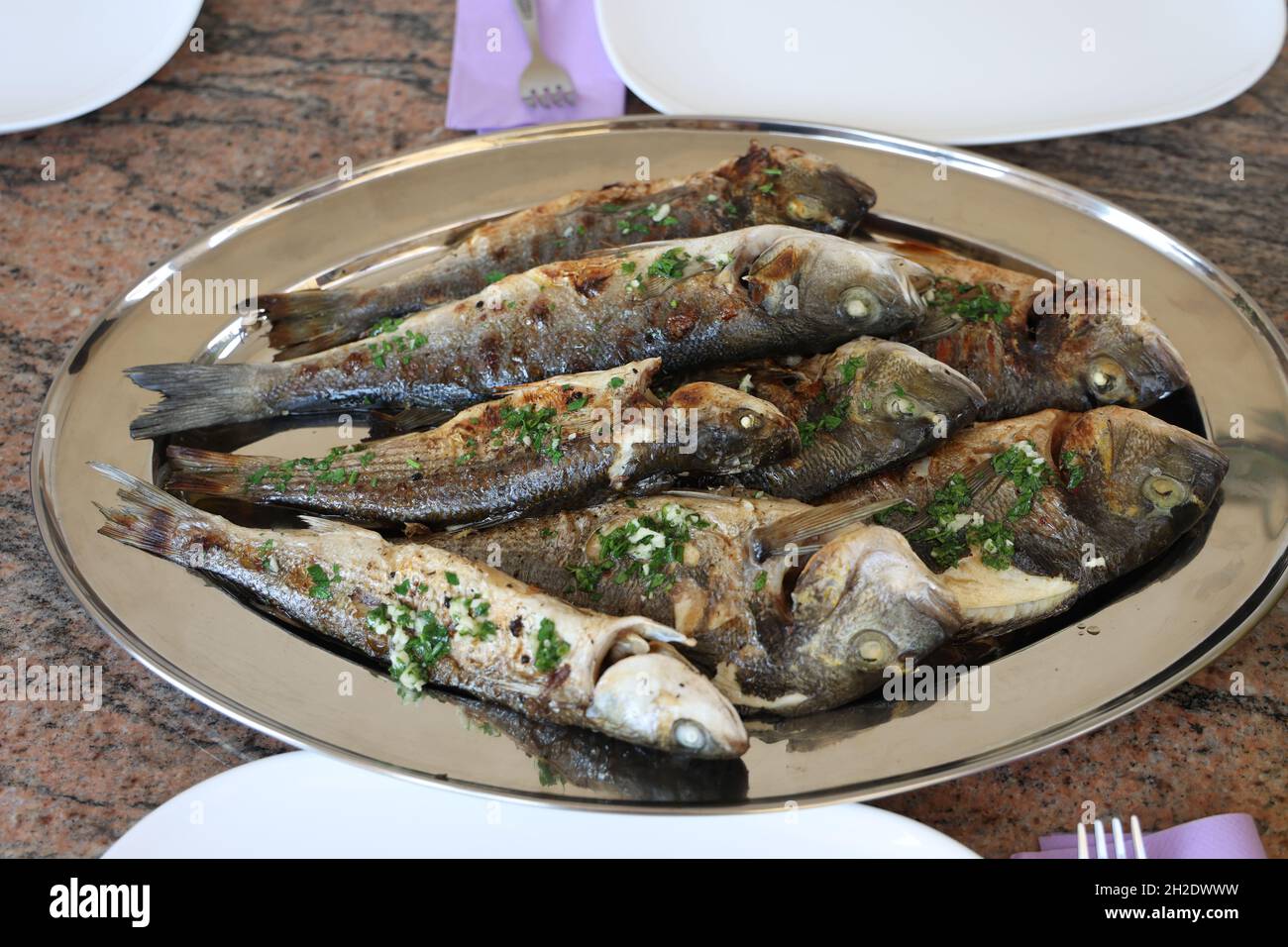 Top view shot of grilled sea fish in an oval metal plate on the table ...
