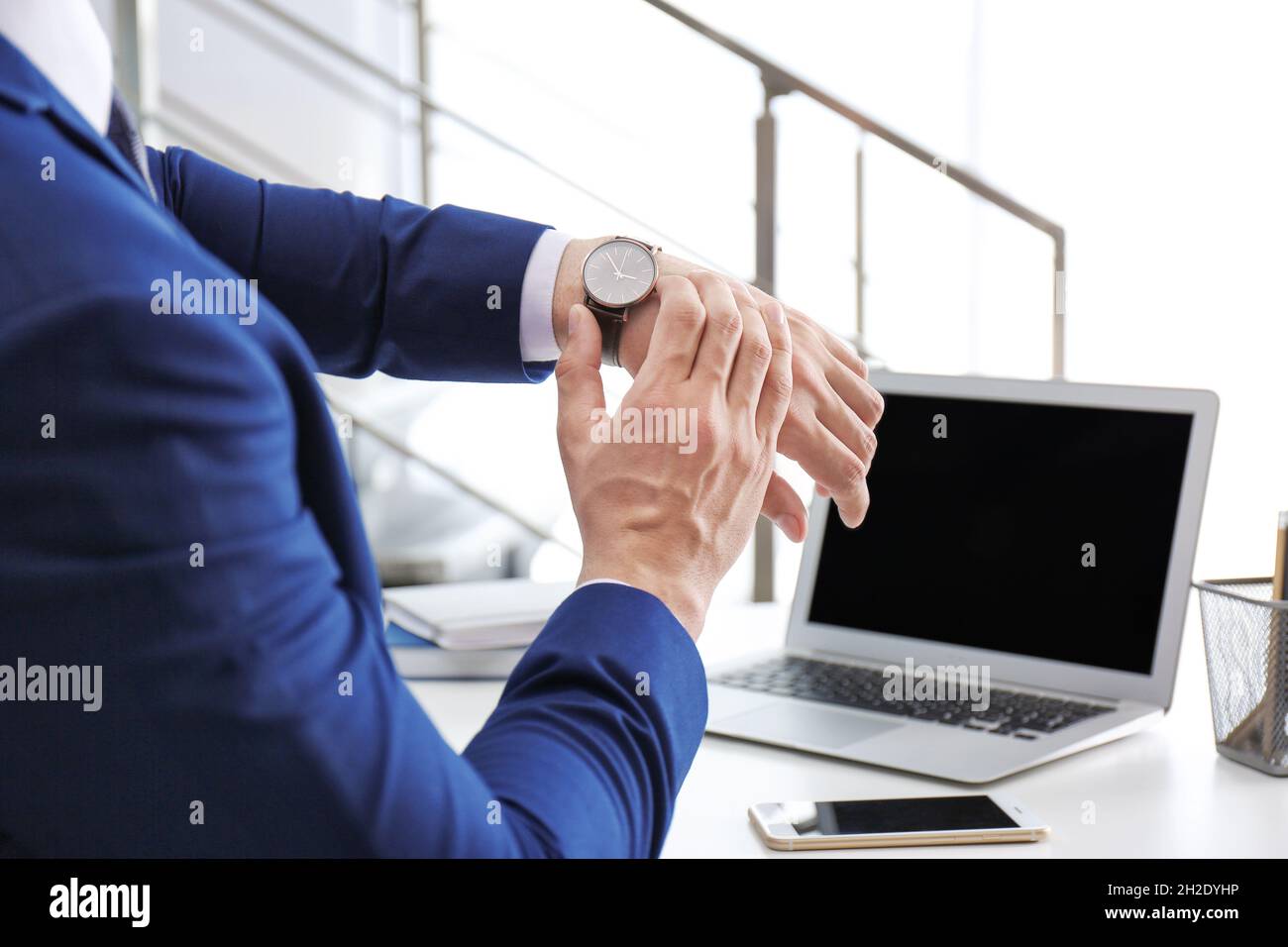 Young businessman checking time on his wristwatch at workplace. Time ...