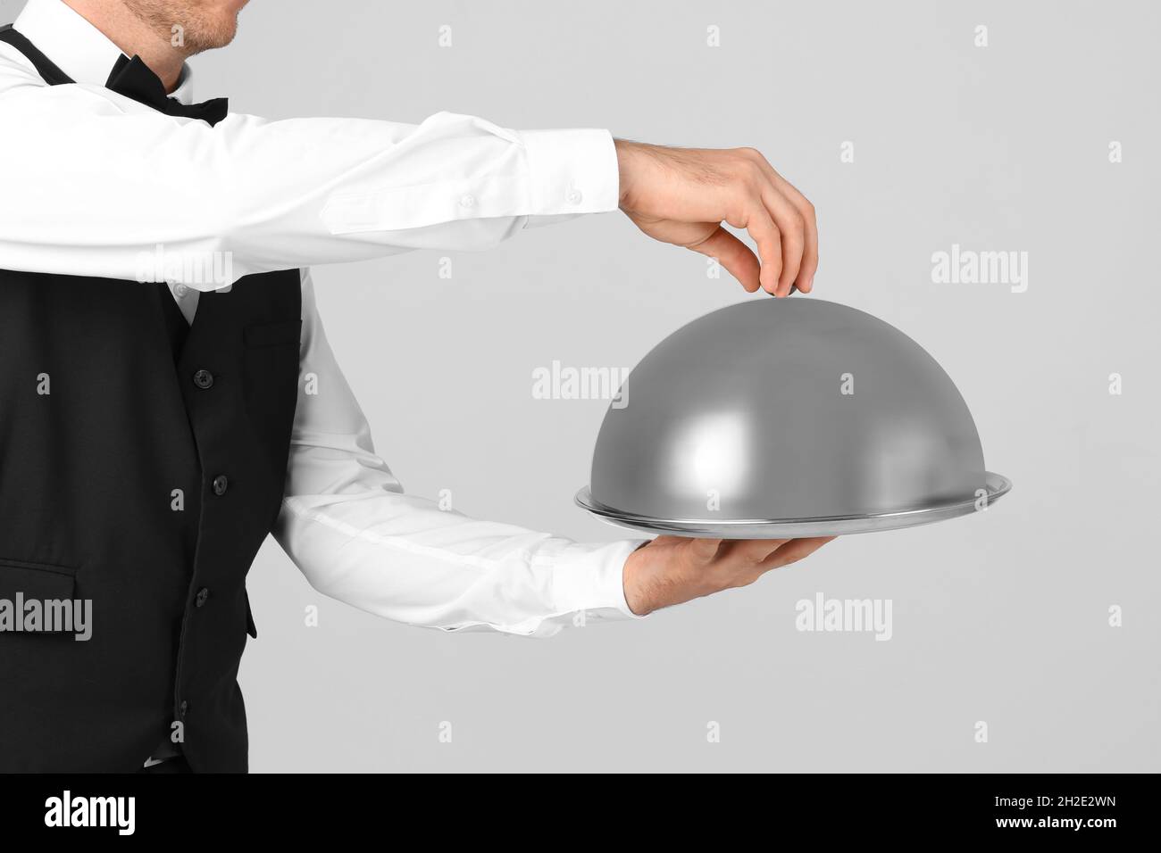 Waiter holding metal tray with lid on light background Stock Photo - Alamy
