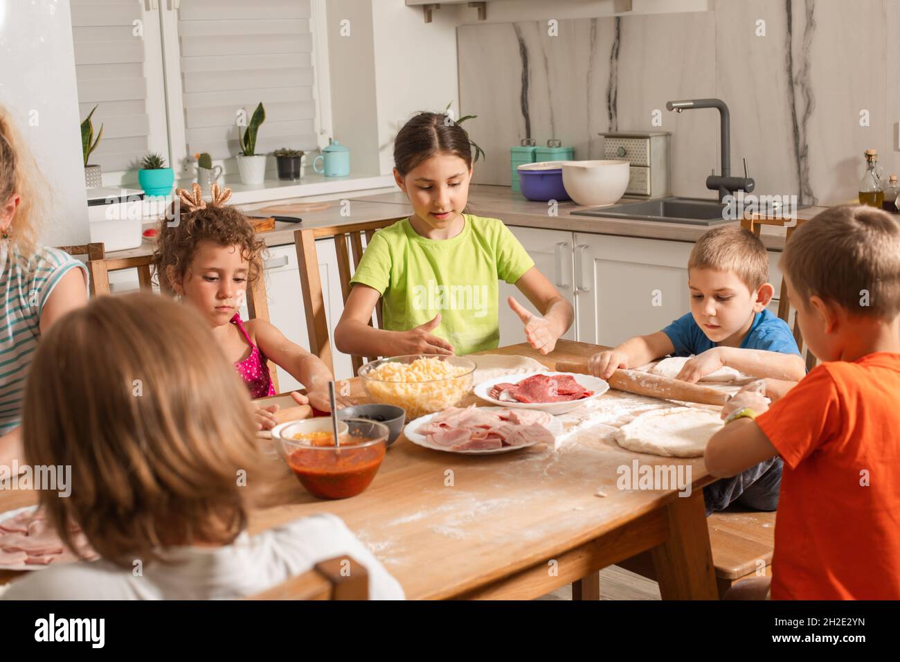 Happy kids sit at a table in the kitchen and make pizza Stock Photo - Alamy