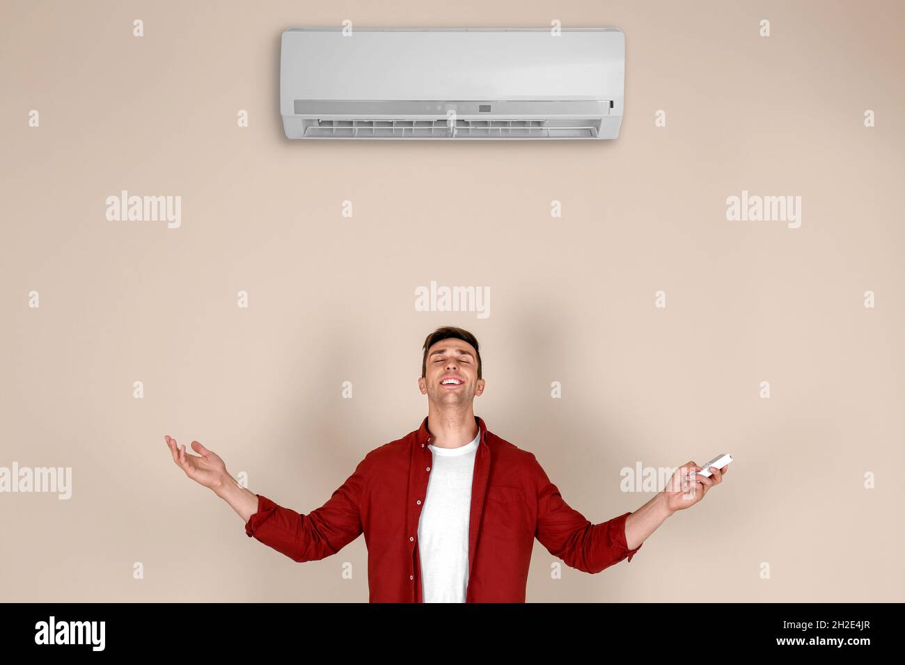 Young man operating air conditioner on color background Stock Photo - Alamy