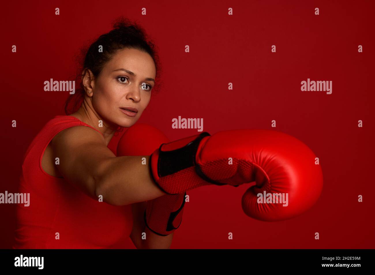 Determined boxer female athlete fights in red boxing gloves on a red ...