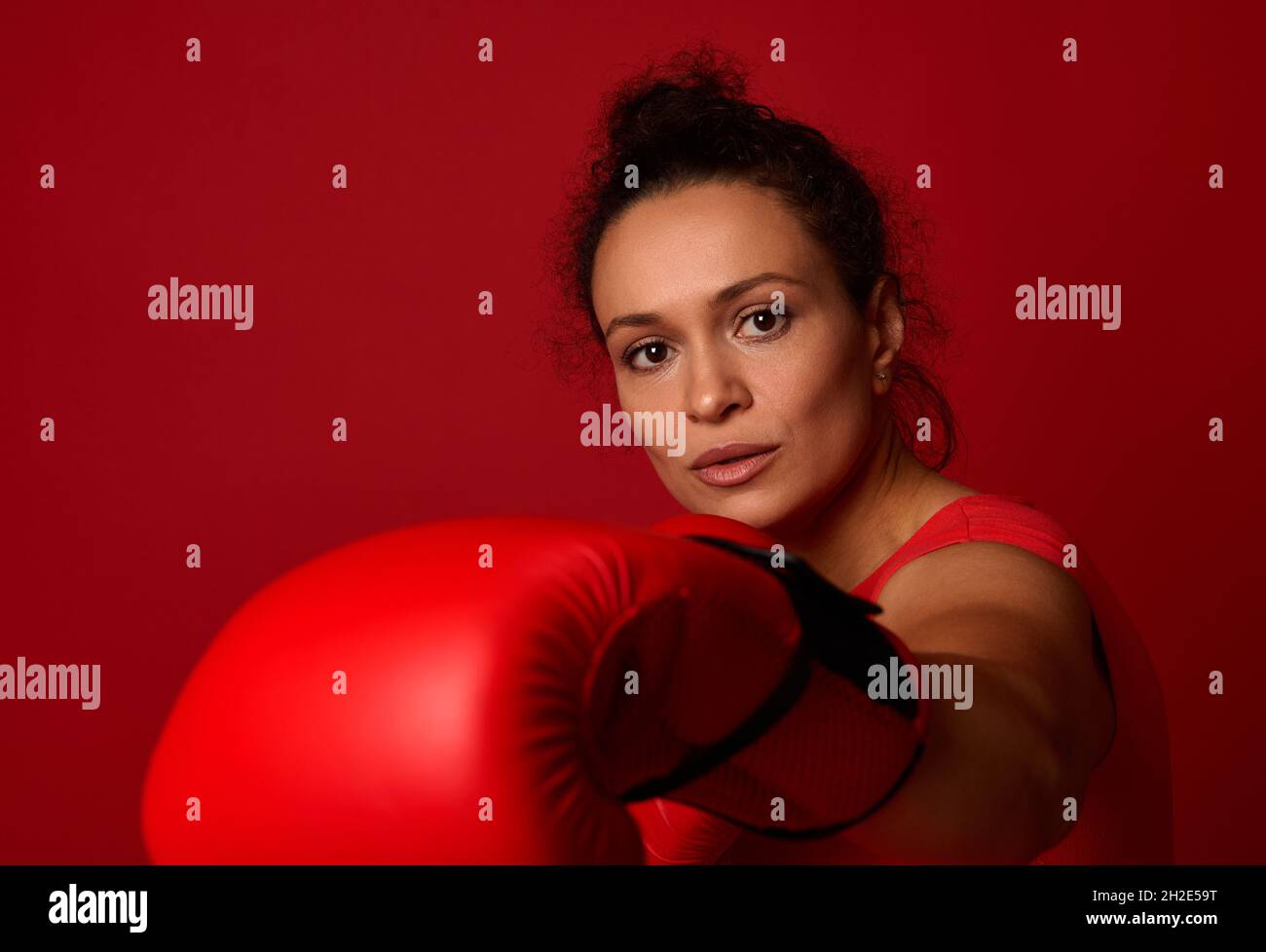 Close-up portrait of concentrated sports woman boxer wearing red boxing ...
