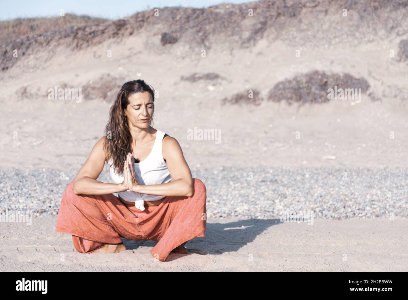 Woman on the beach doing the yoga posture malasana, after sunrise, with ...