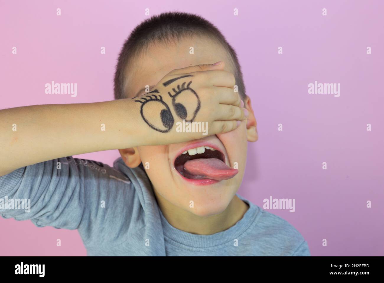 Cheerful Caucasian boy covering his face with his hand with a silly eye ...