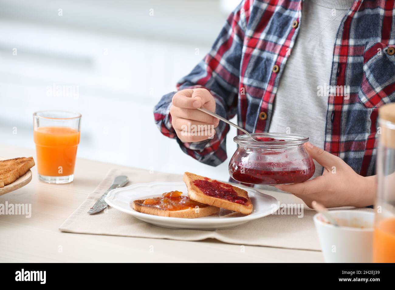 Cute little boy spreading jam onto tasty toasted bread at table Stock ...