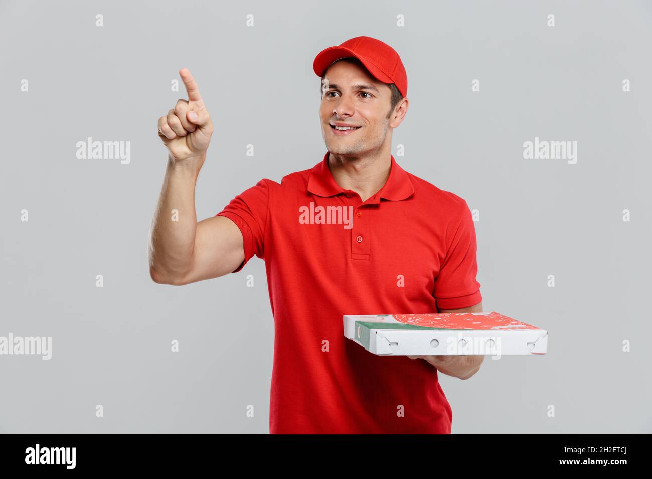 Young delivery man pointing finger upward while posing with pizza box ...