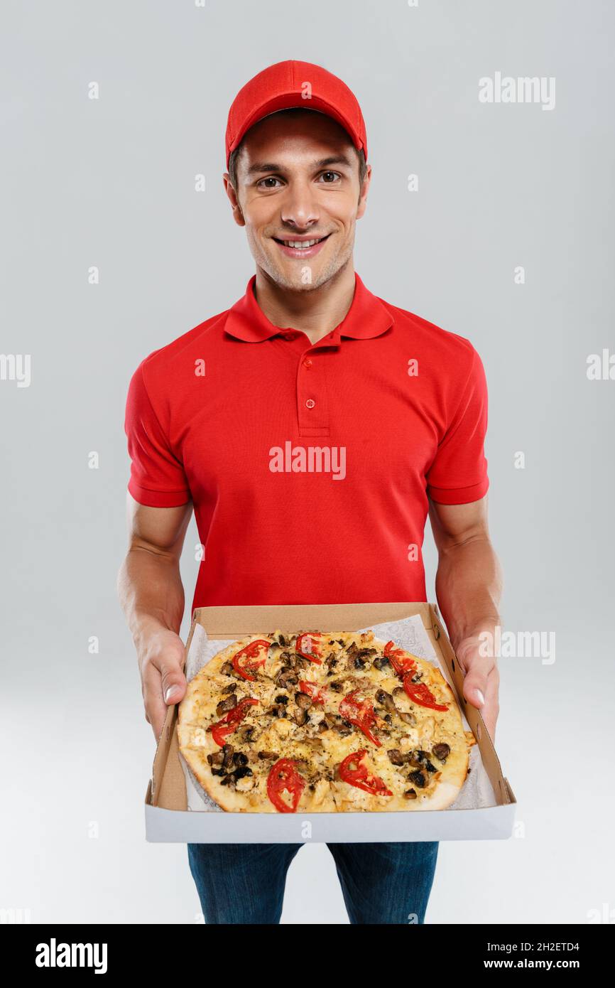 Young delivery man in uniform smiling while showing pizza isolated over ...