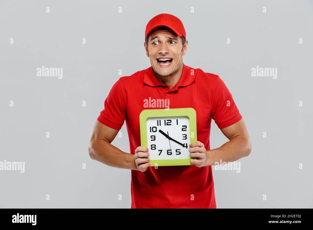 Young shocked delivery man in uniform screaming while showing clock ...